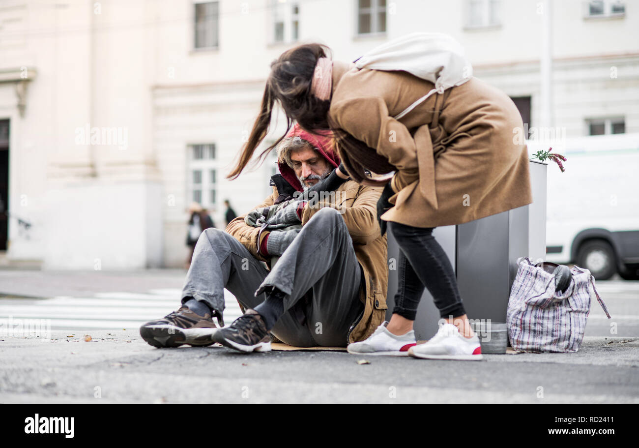 Young Woman Giving Money To Homeless Beggar Man Sitting In City Stock