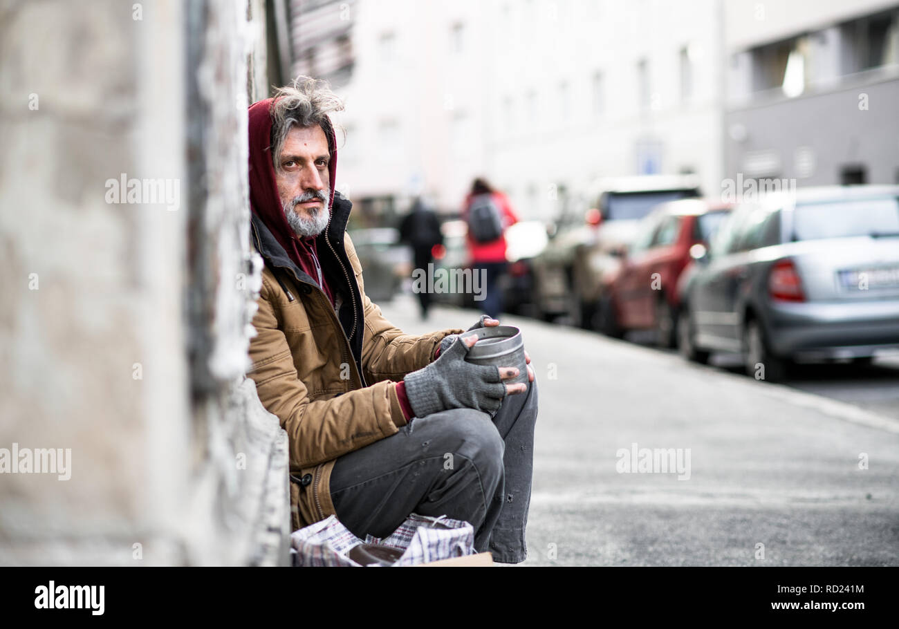 Homeless beggar man sitting outdoors in city asking for money donation ...