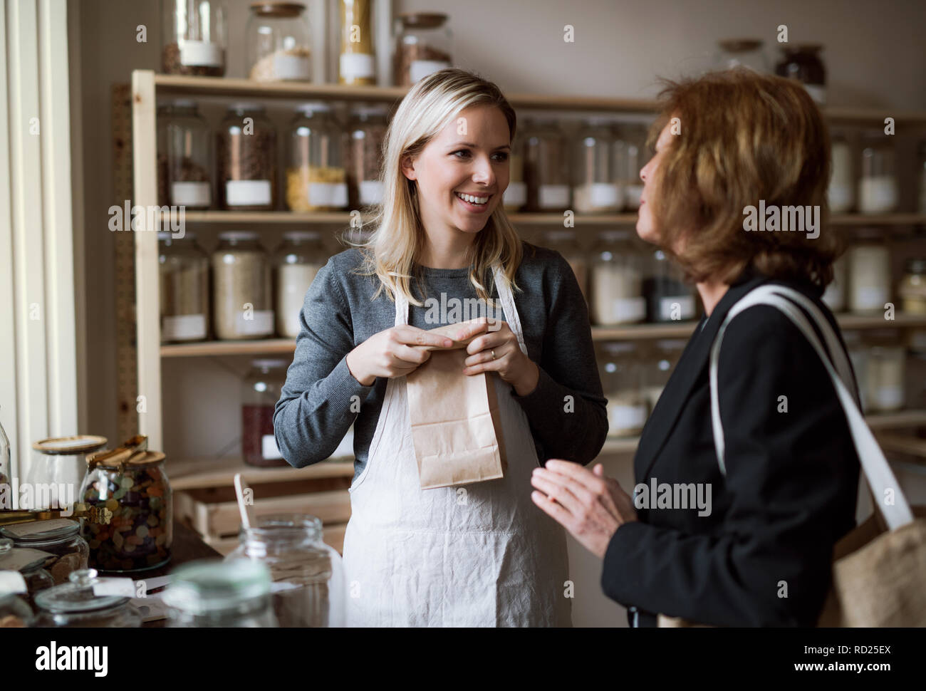 A female shop assistant serving a senior customer in a zero-waste shop ...