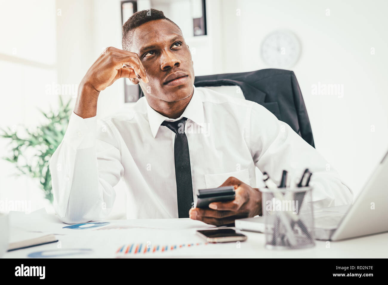 Pensive African businessman working on calculator in modern office and ...