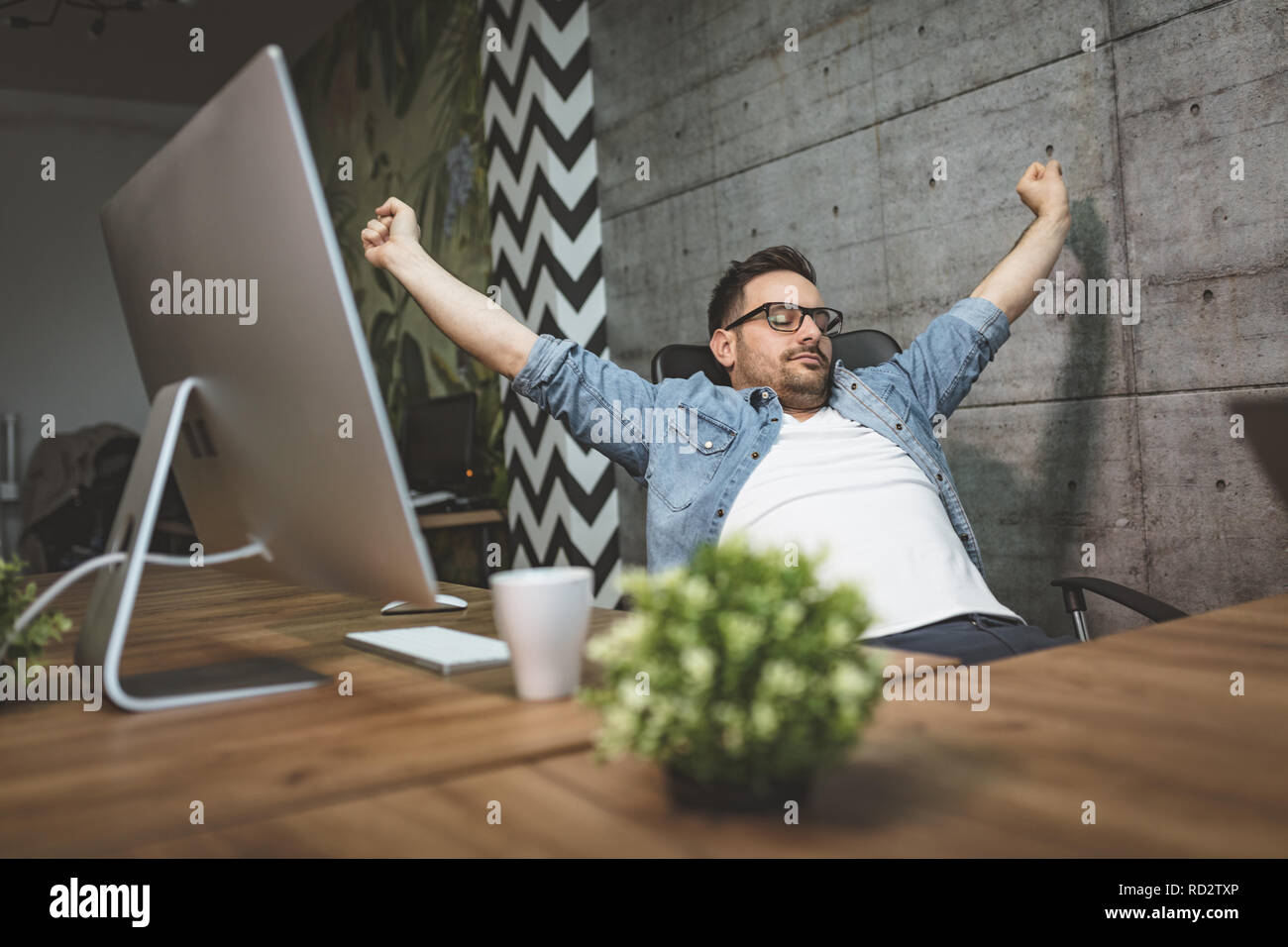 Young handsome overworked businessman sitting in the office stretching ...