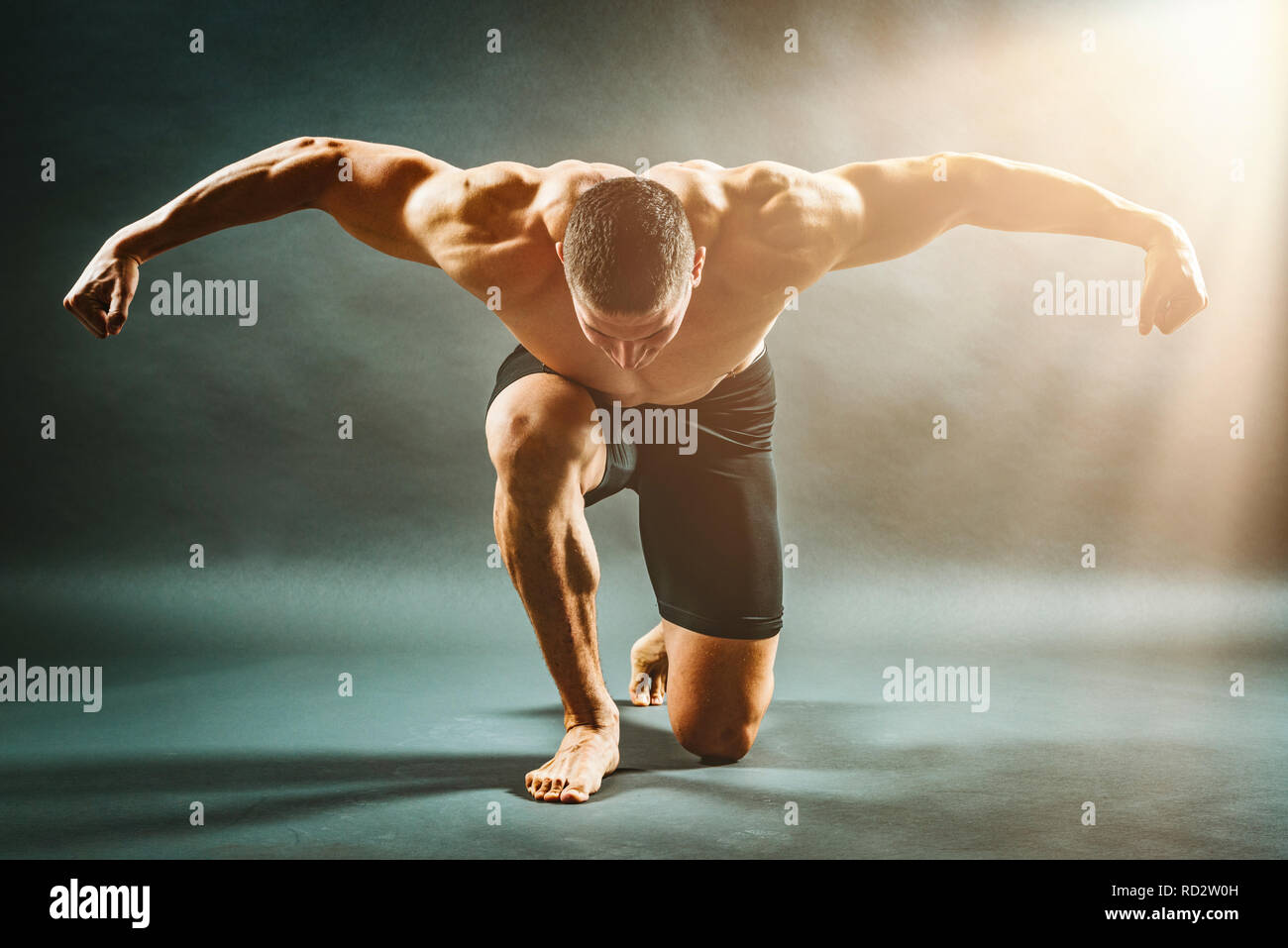 Muscular male is standing on one knee and showing his muscles, threw up ...