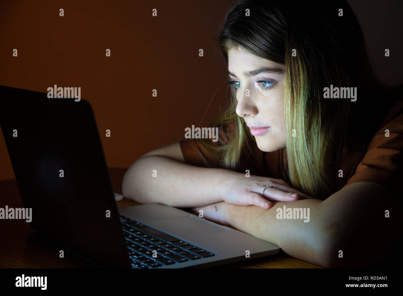 A pretty teenage girl staring at her laptop and being lit by the glow ...