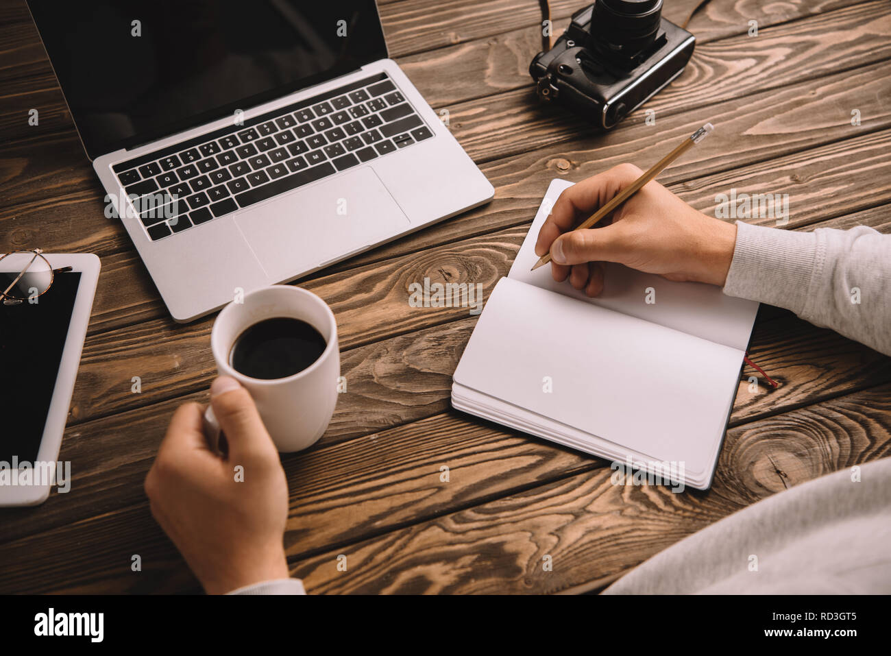 cropped view of male photographer writing in notebook at table with cup ...