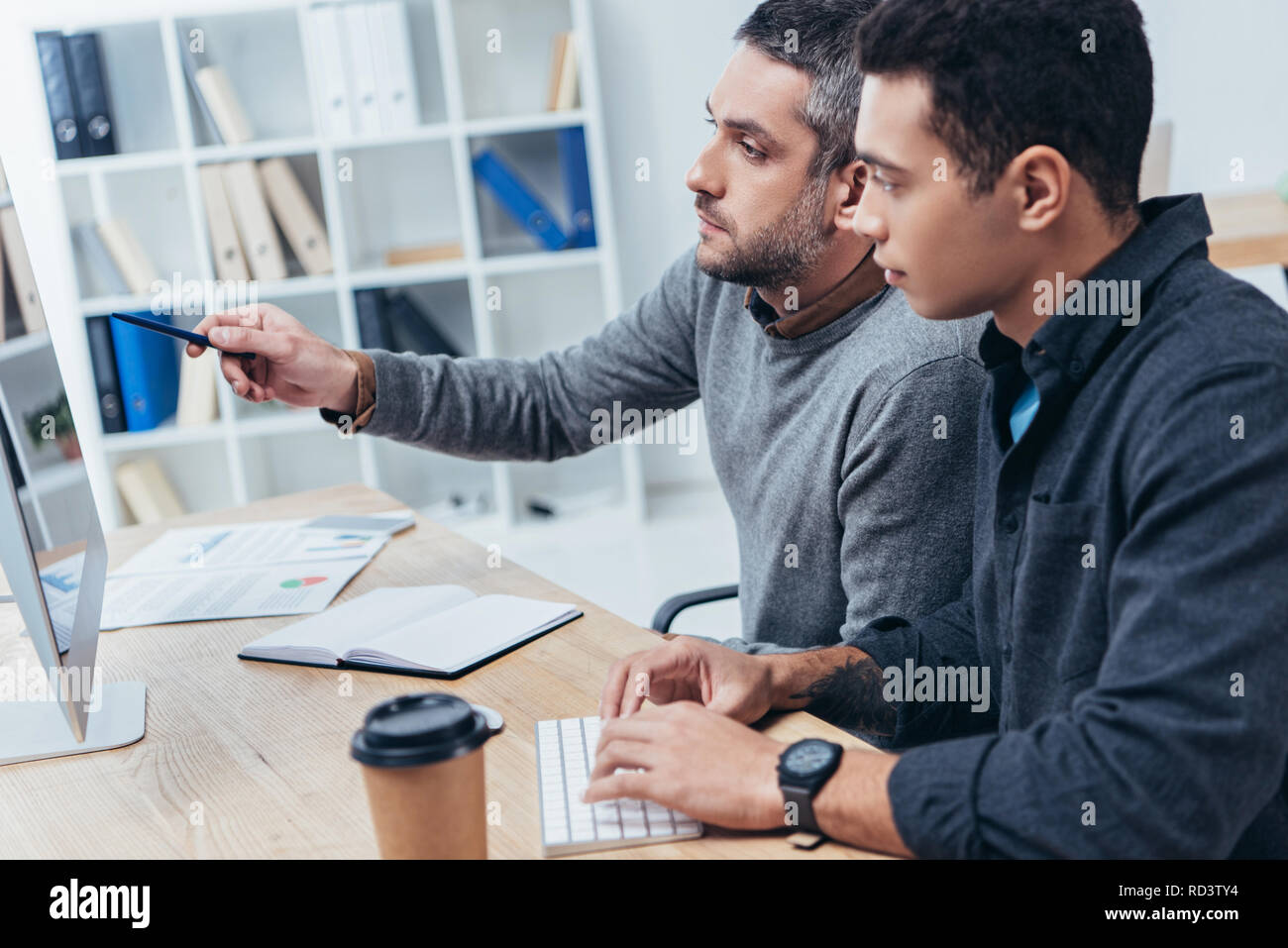 colleagues typing on keyboard and pointing at screen while working with ...