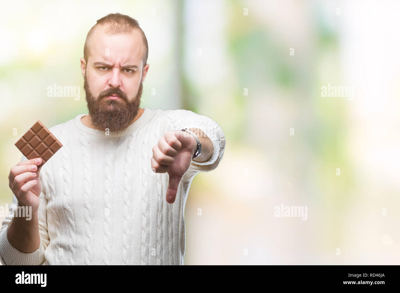 Young hipster man eating chocolate bar over isolated background with ...