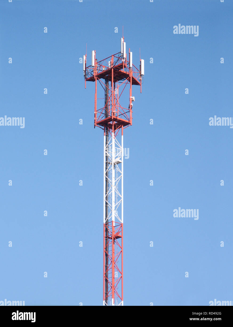 High red and white cellular tower frame with aerials on top over clear blue sky in sunny day ...