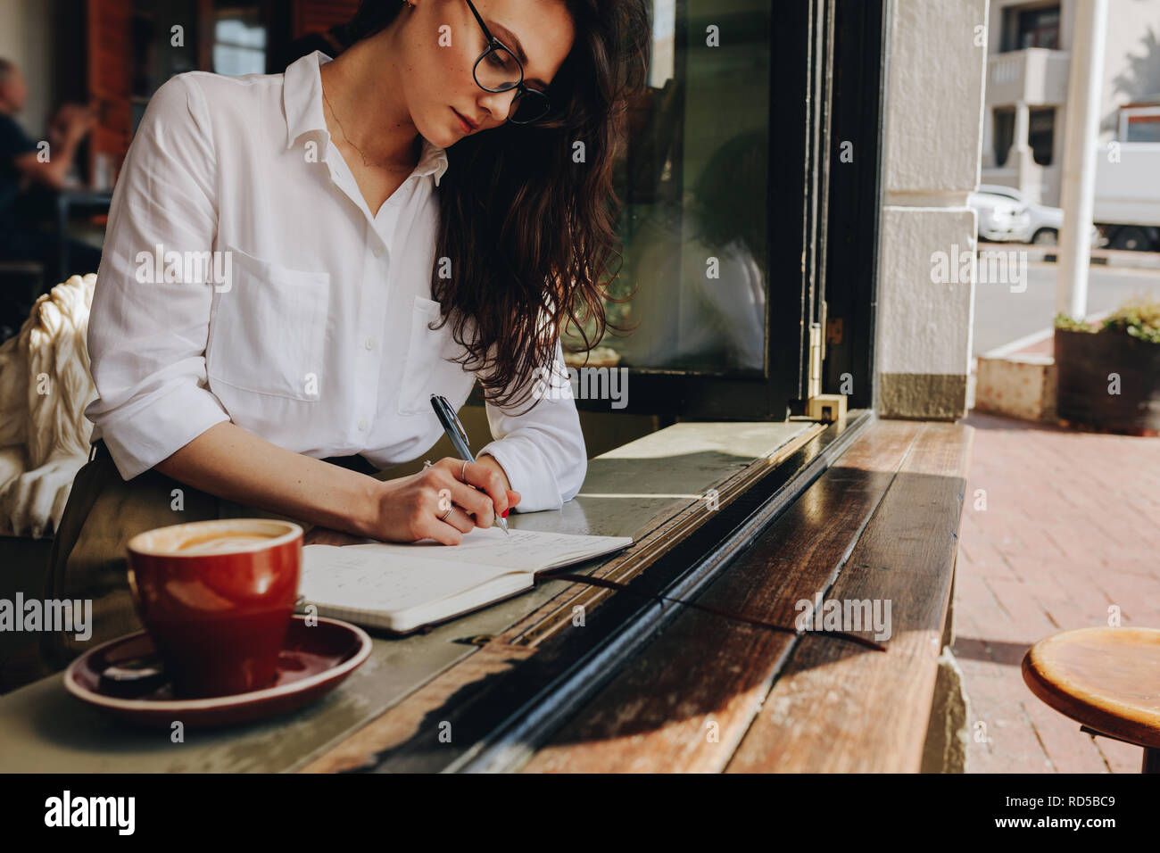 Female sitting by window at cafe writing in a book with cup of coffee ...
