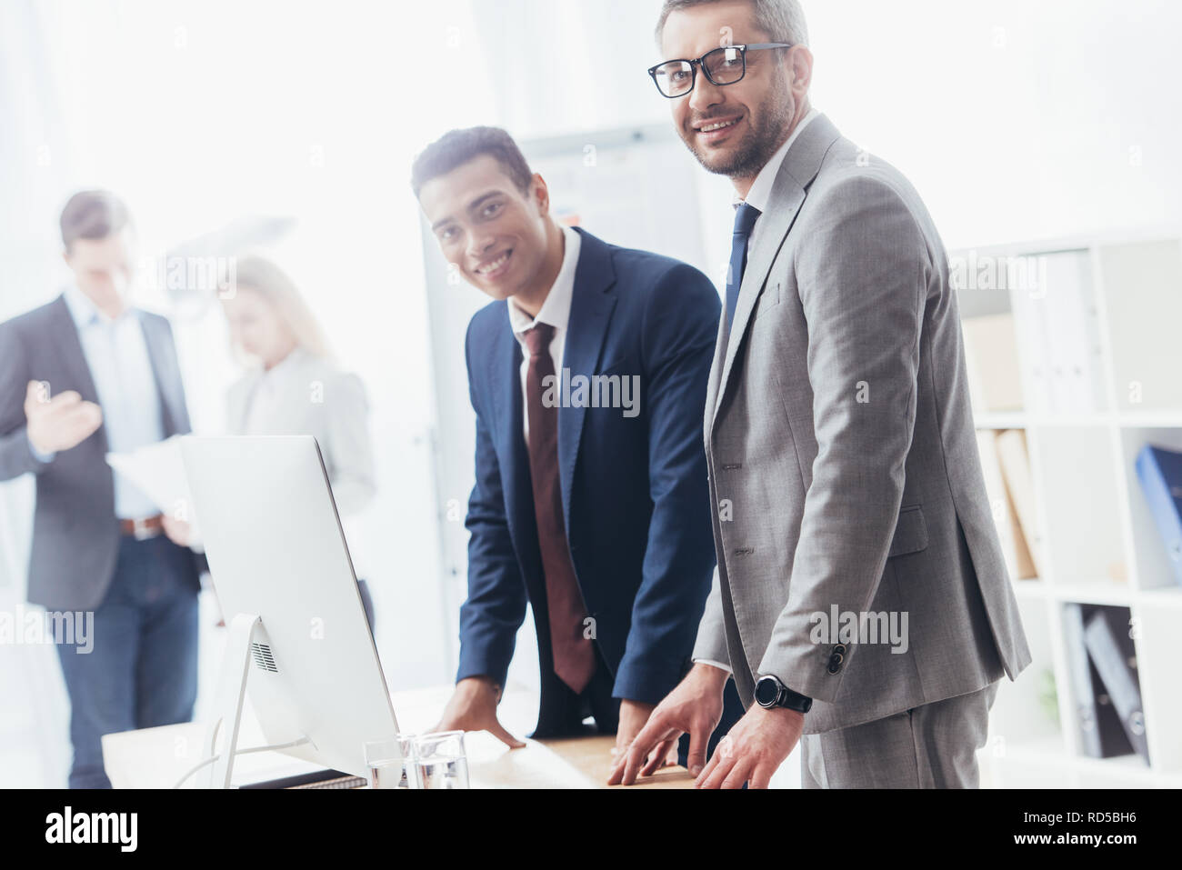 happy businessmen smiling at camera while leaning at table with desktop ...