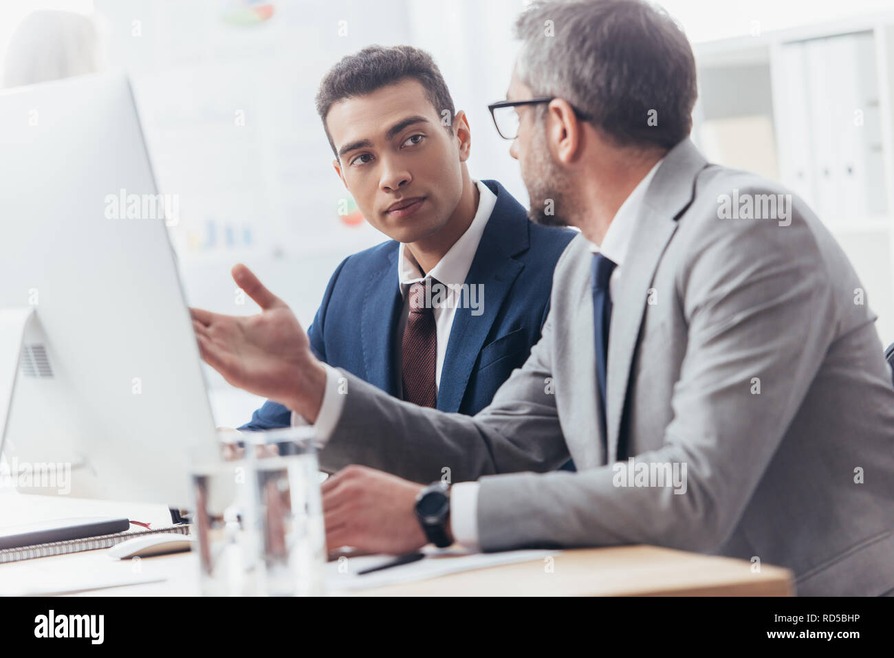 two professional businessmen using desktop computer and discussing ...