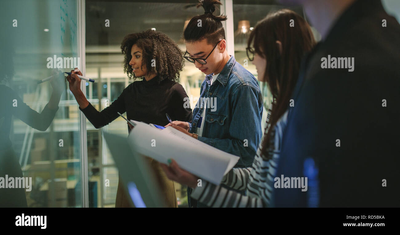 Female student writing on glass board in classroom. Girl writing on ...