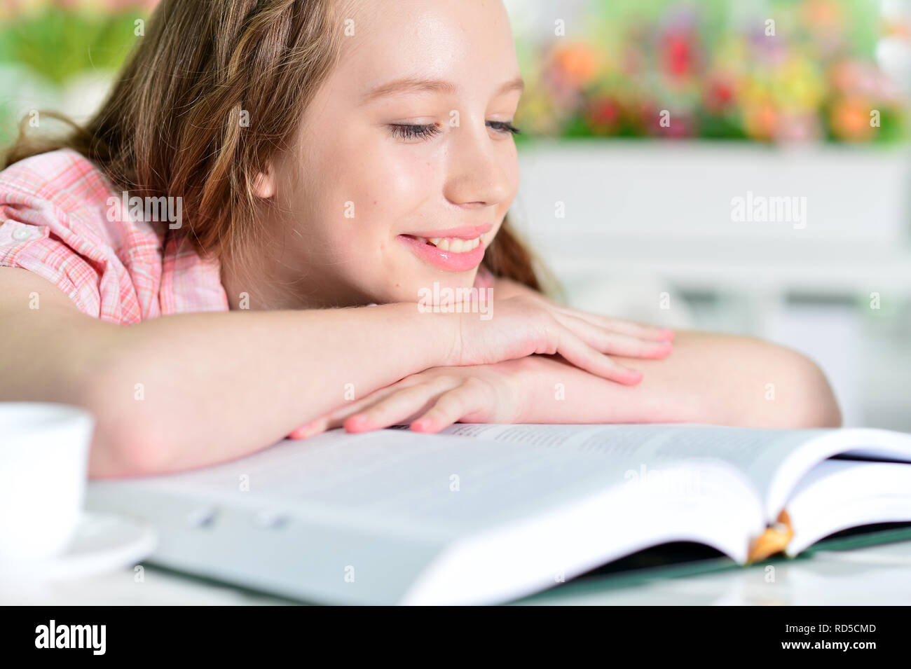 Cute schoolgirl sitting at table and reading Stock Photo - Alamy