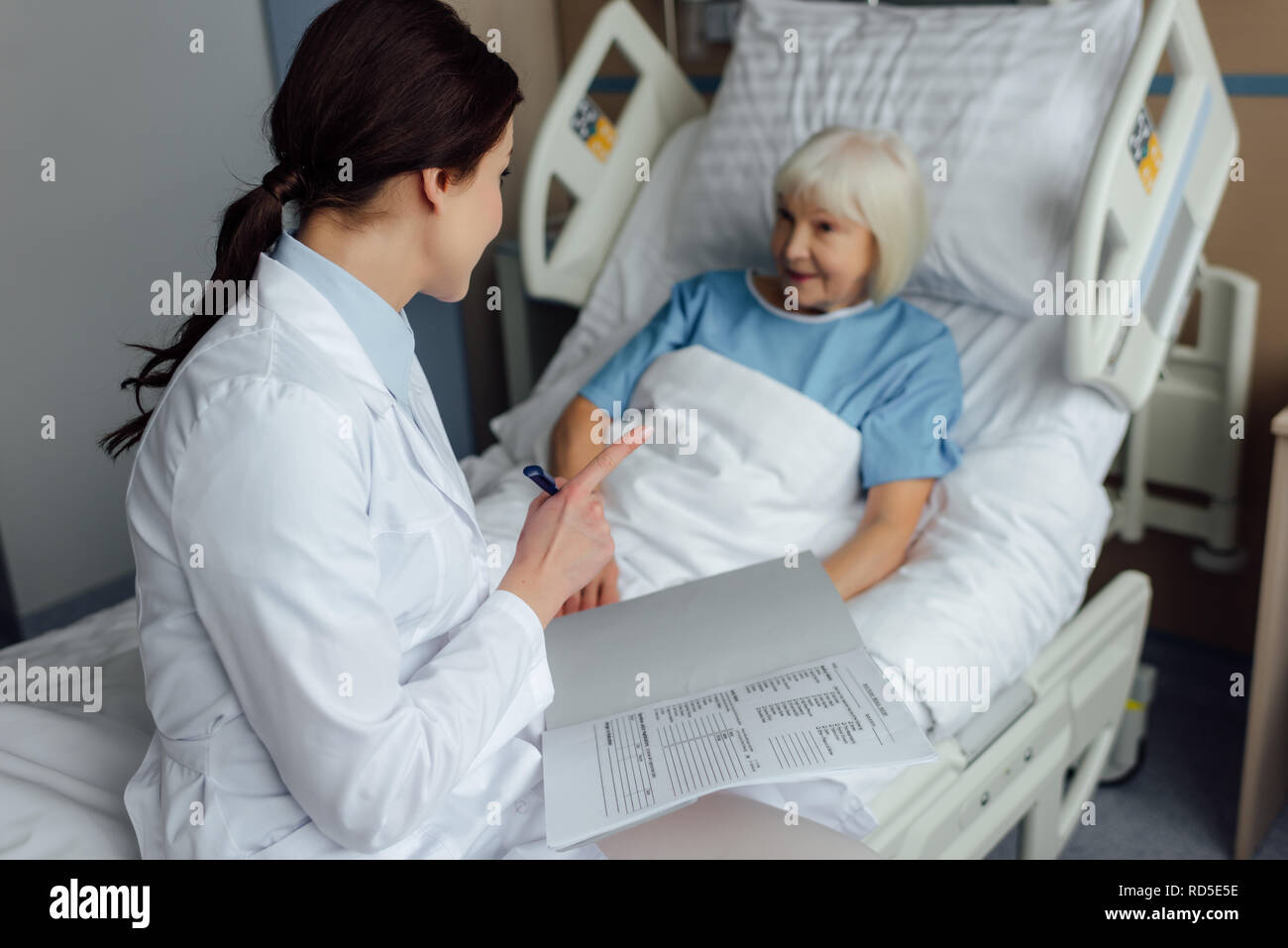 female doctor sitting on bed, holding diagnosis and pointing with ...