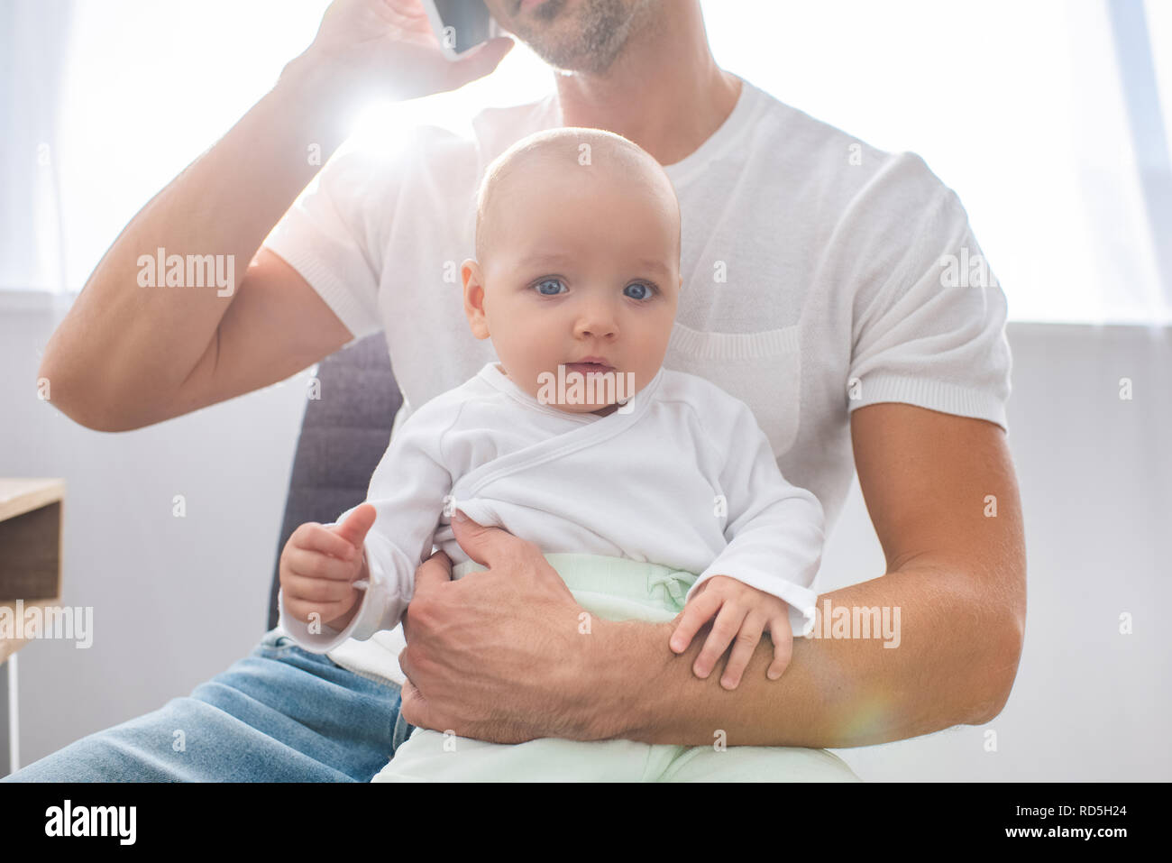 father sitting on chair, talking on smartphone and holding adorable ...