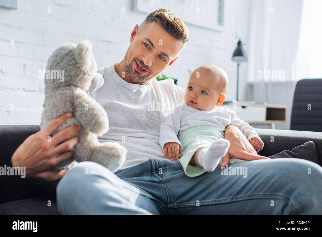 father sitting on couch with adorable baby daughter and playing with ...