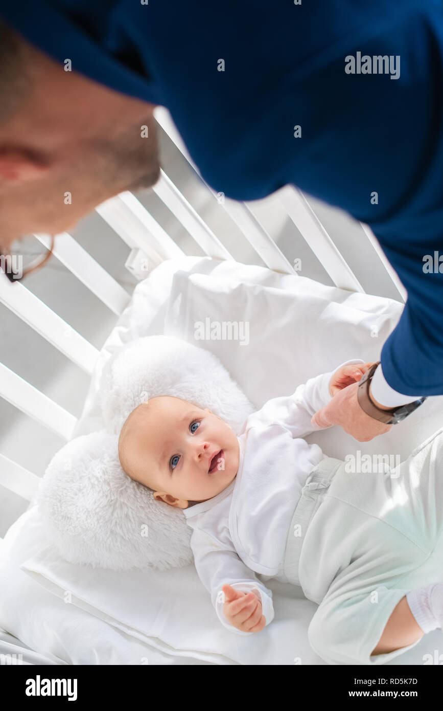 overhead view of father in suit holding hand of infant daughter in baby ...