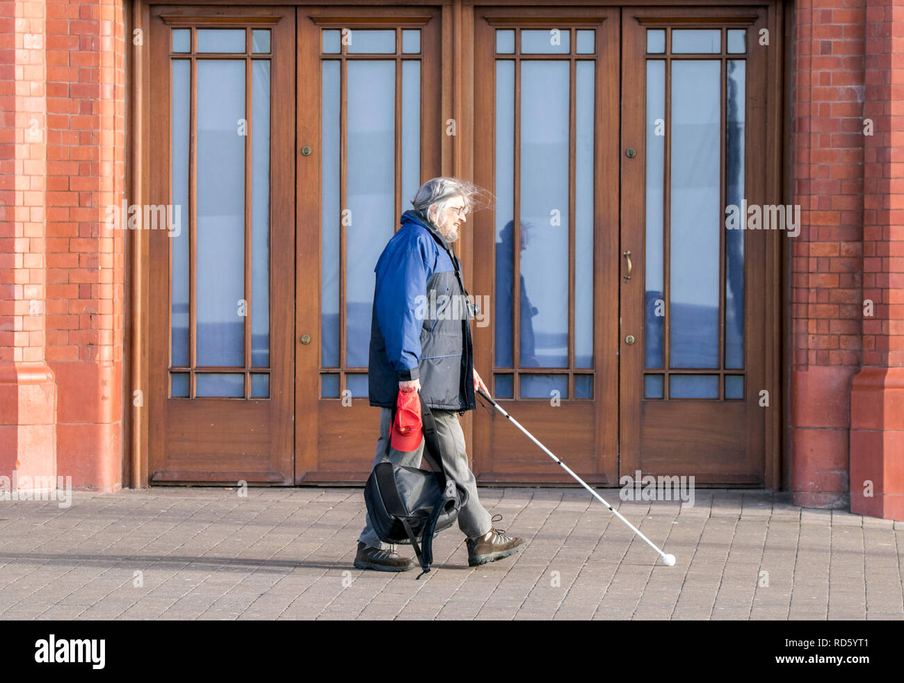 A blind man using a specialized walking stick to cross a zebra crossing ...