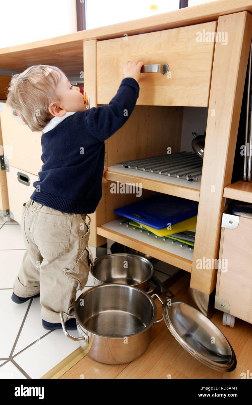 Little boy, 10 months, taking cooking pots from a cupboard in the ...