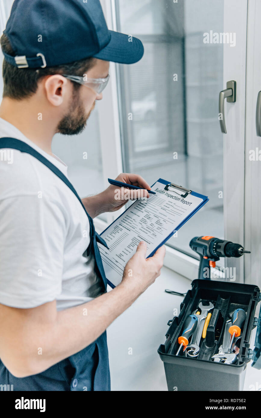rear view of adult repairman writing in clipboard and checking window ...