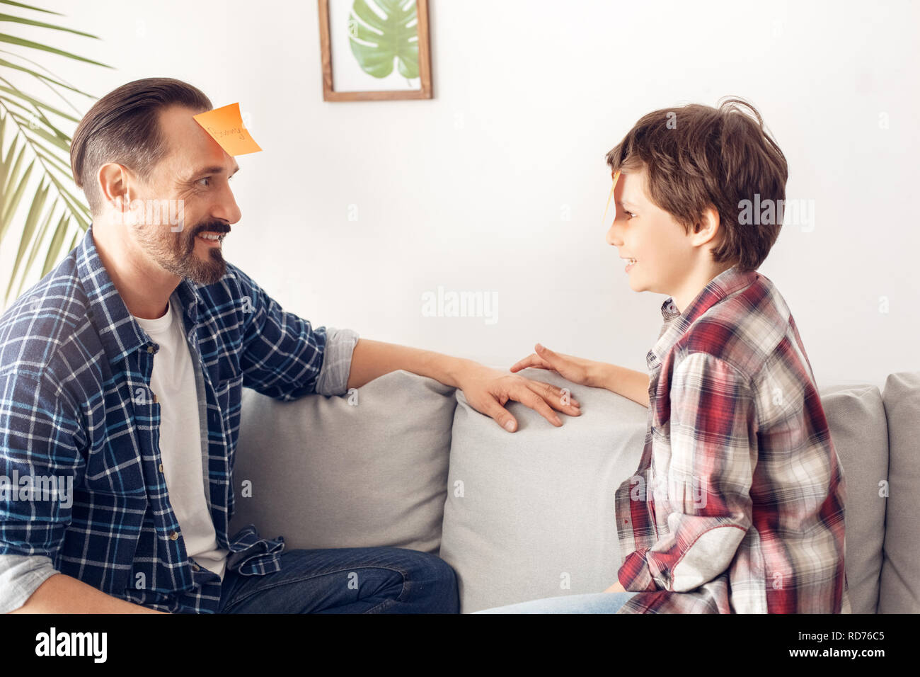 Father and little son at home sitting on sofa playing forehead ...