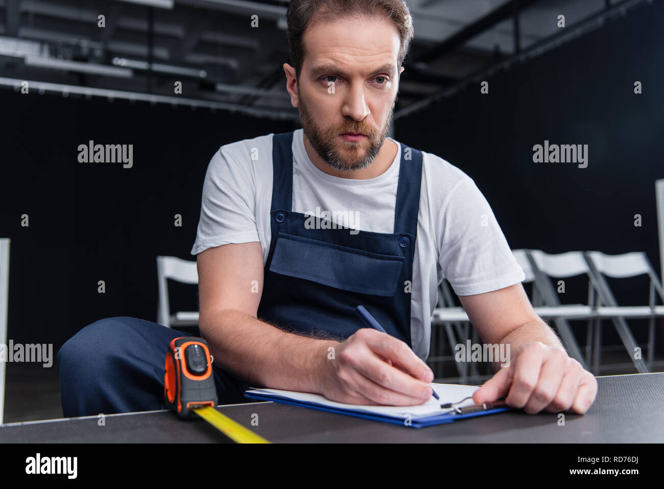 serious male handyman making measurements and writing in clipboard ...