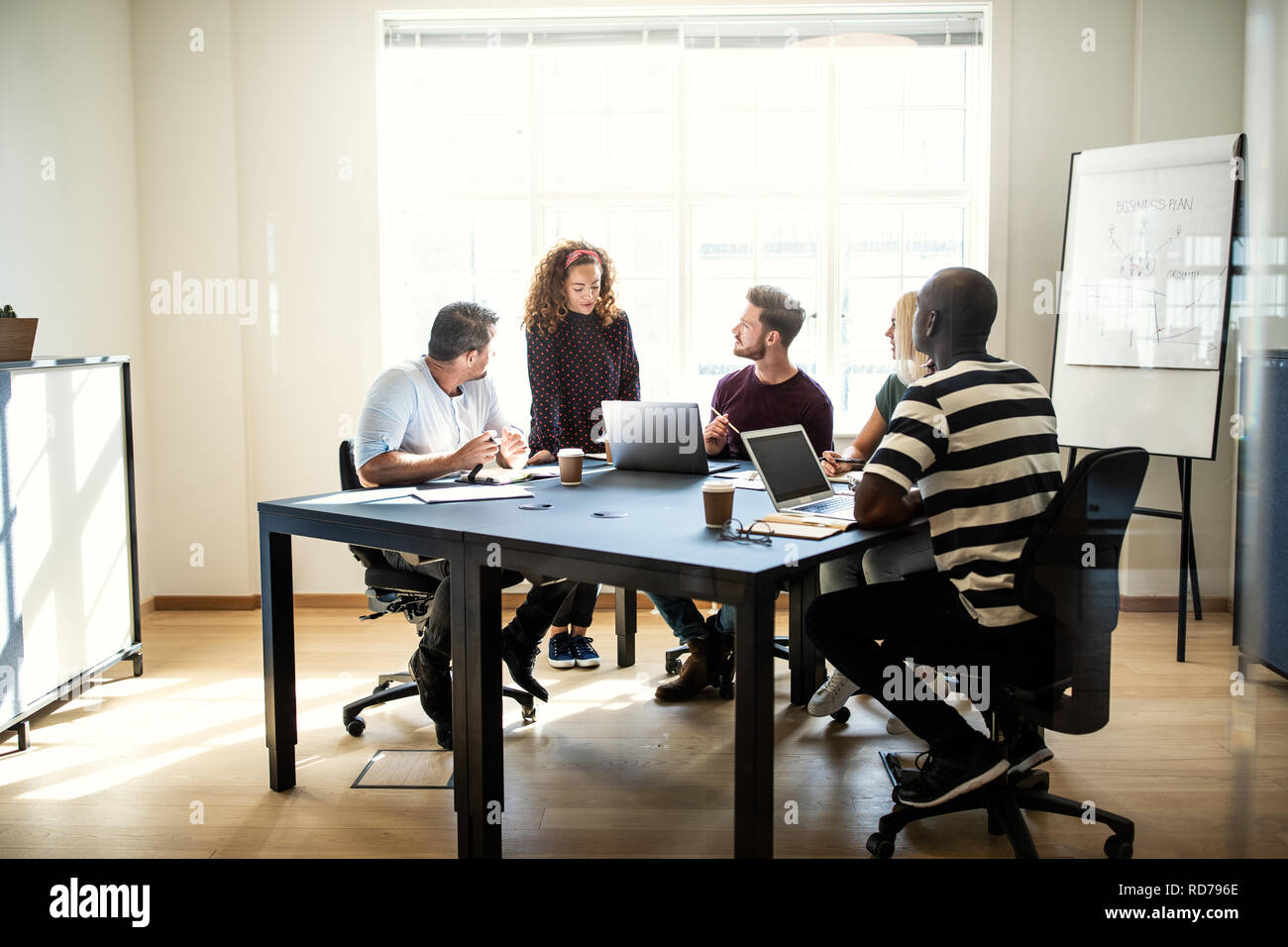 Diverse group of young designers discussing work together while sitting ...
