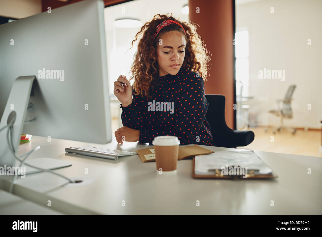 Focused young businesswoman sitting alone at her desk in an empty ...