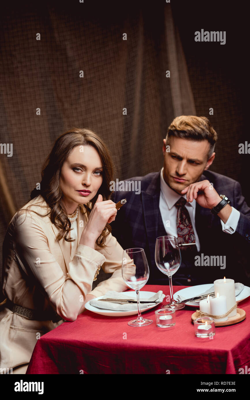 beautiful woman sitting at table and smoking cigar while having ...