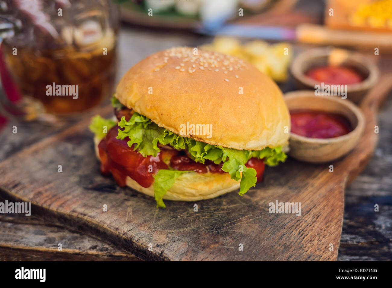 Closeup of fresh burger with French fries on wooden table with bowls of ...