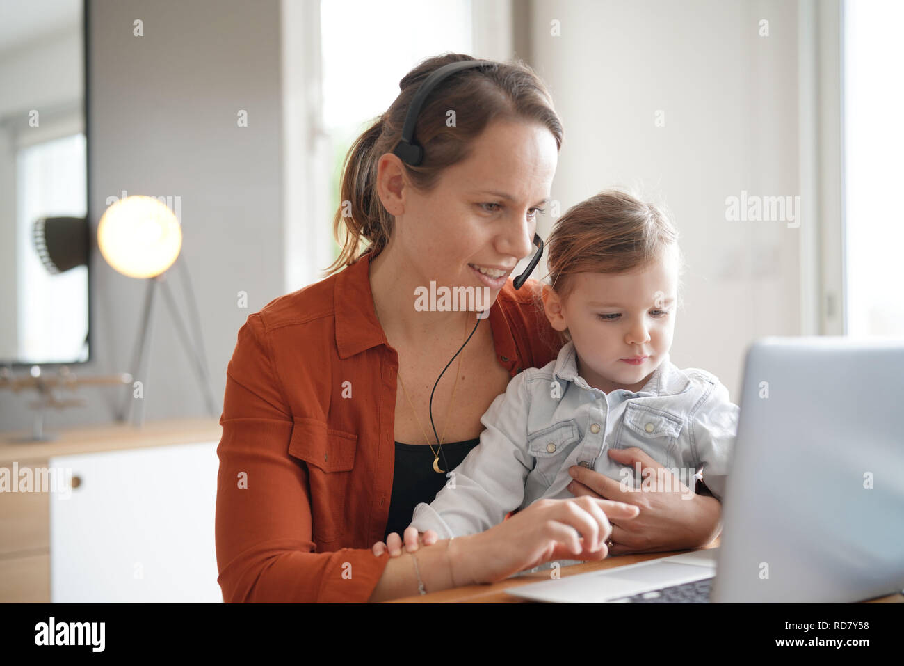 Mother working from home on computer with her young daughter Stock ...