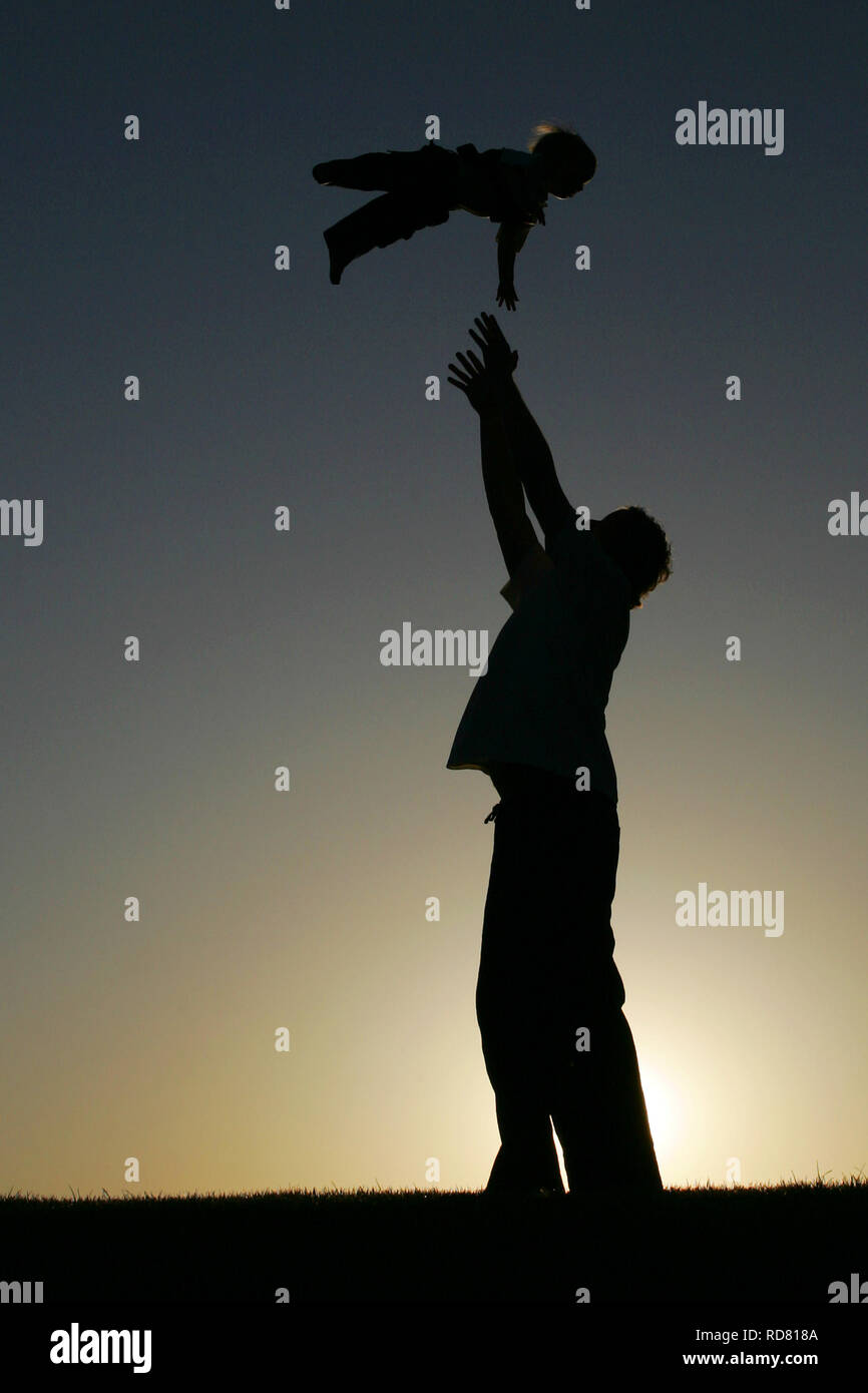A silhouette of a father throwing his son in the air during a portrait ...