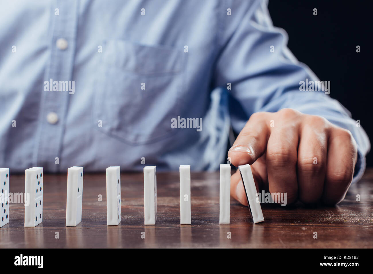 partial view of man pushing domino row on wooden desk Stock Photo - Alamy
