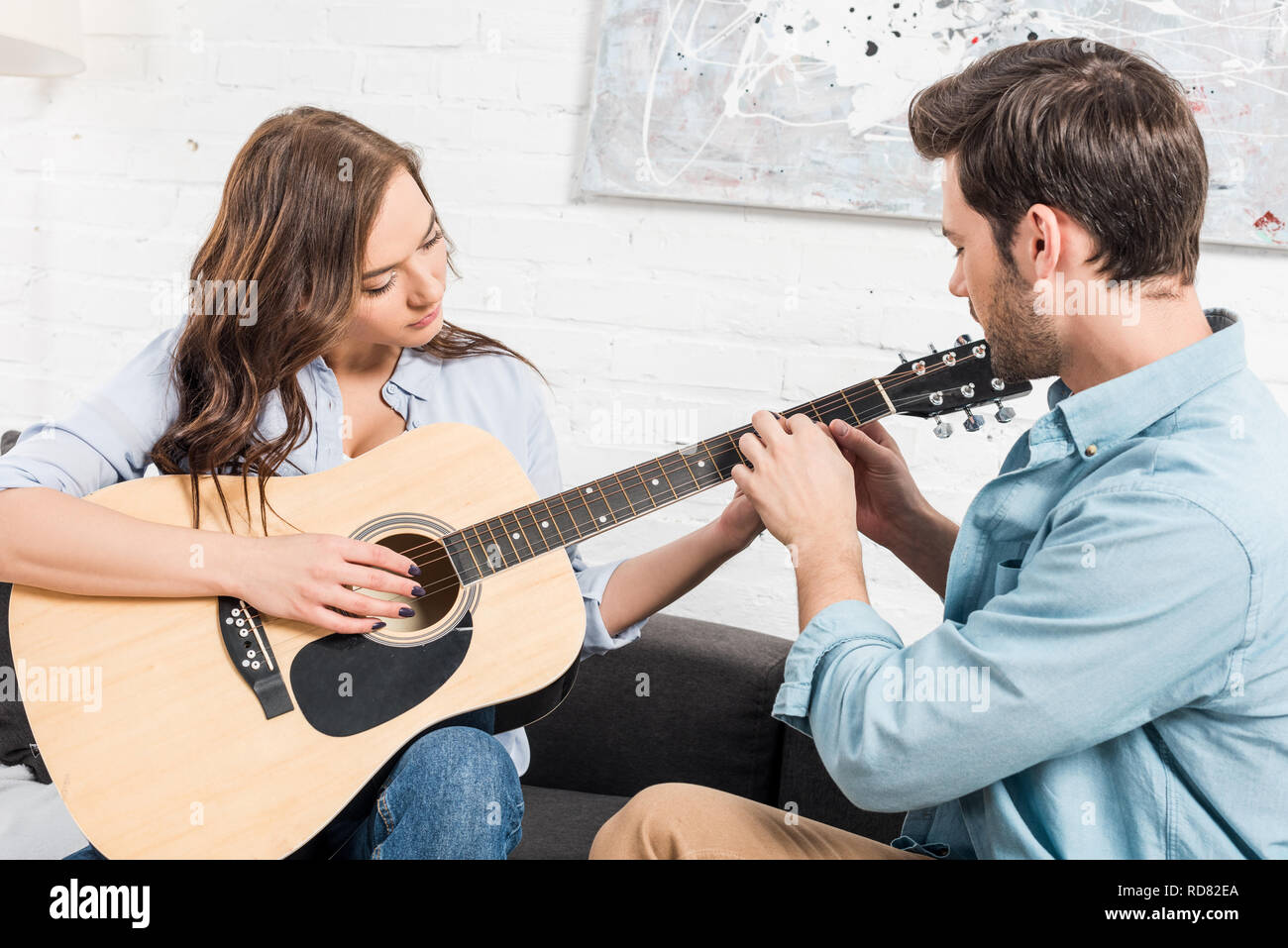 man sitting on couch and teaching woman to play acoustic guitar at home ...
