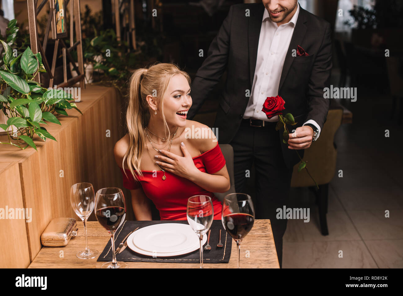 boyfriend giving red rose to surprised girlfriend in restaurant Stock ...