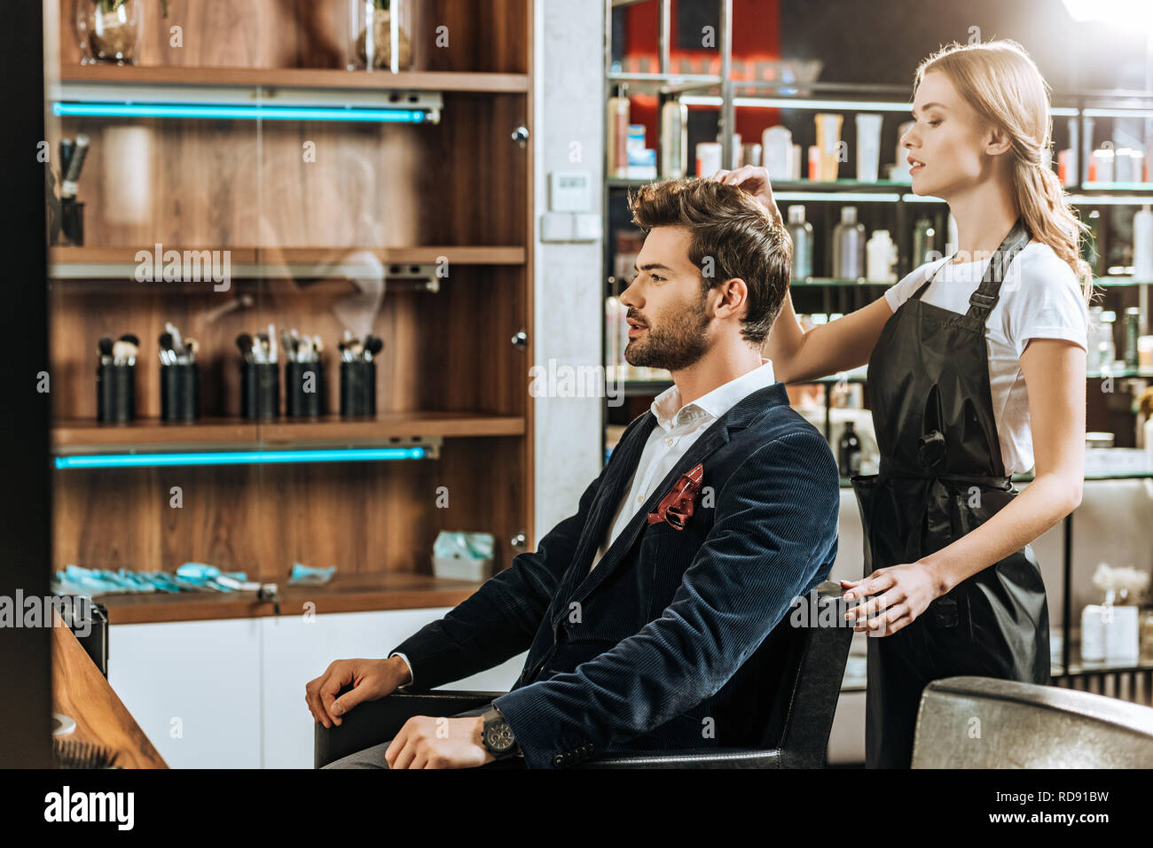 side view of young hairdresser doing hairstyle to handsome male client ...