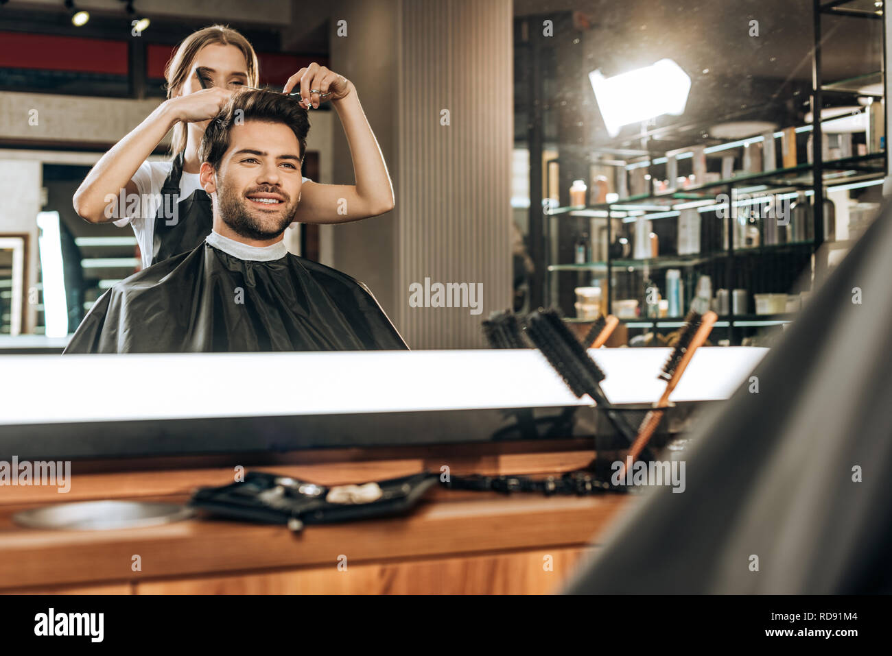 reflection in mirror of young hairdresser cutting hair to handsome ...