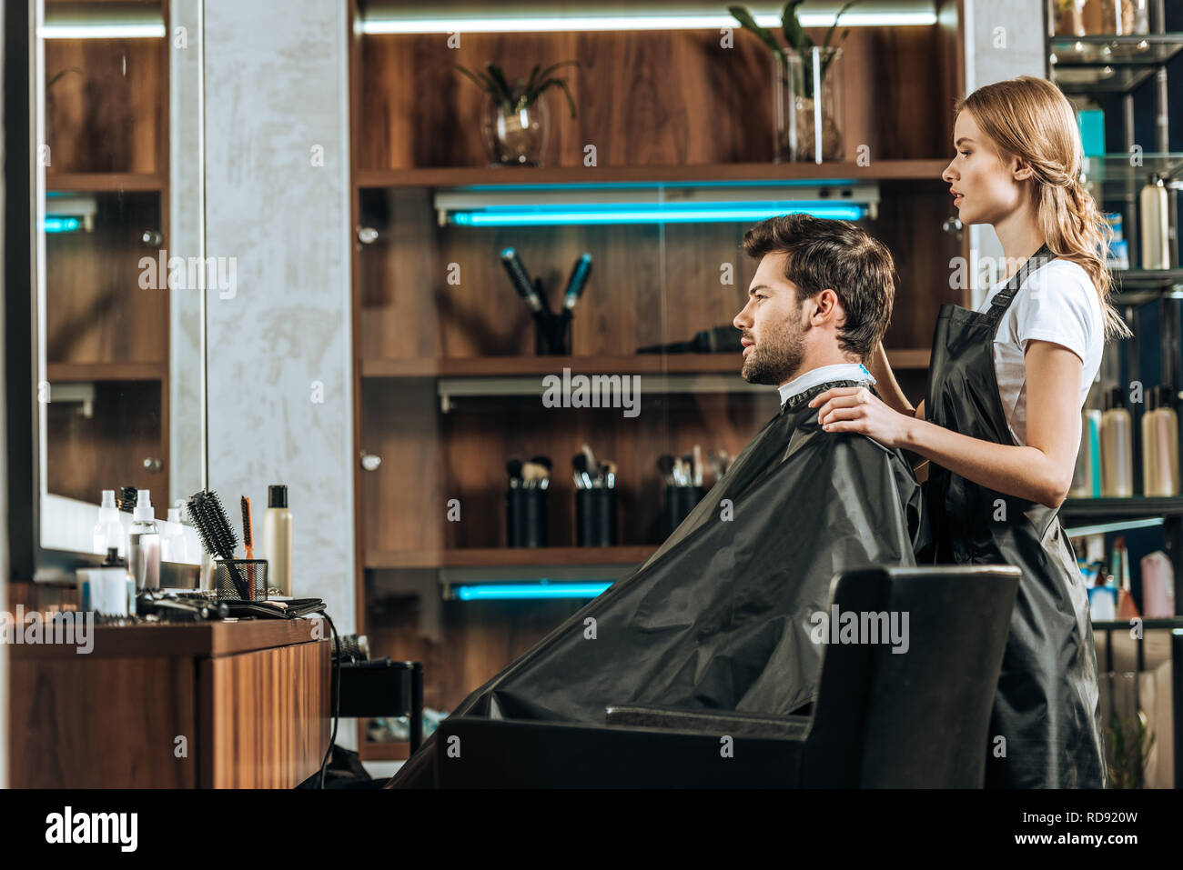 side view of female hairstylist and handsome young man looking at ...