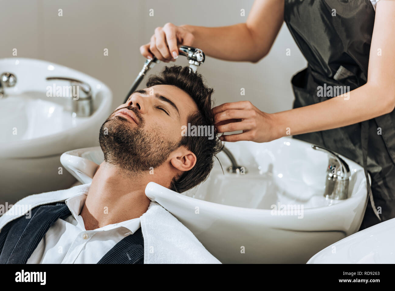 cropped shot of professional hairstylist washing hair to male client in ...