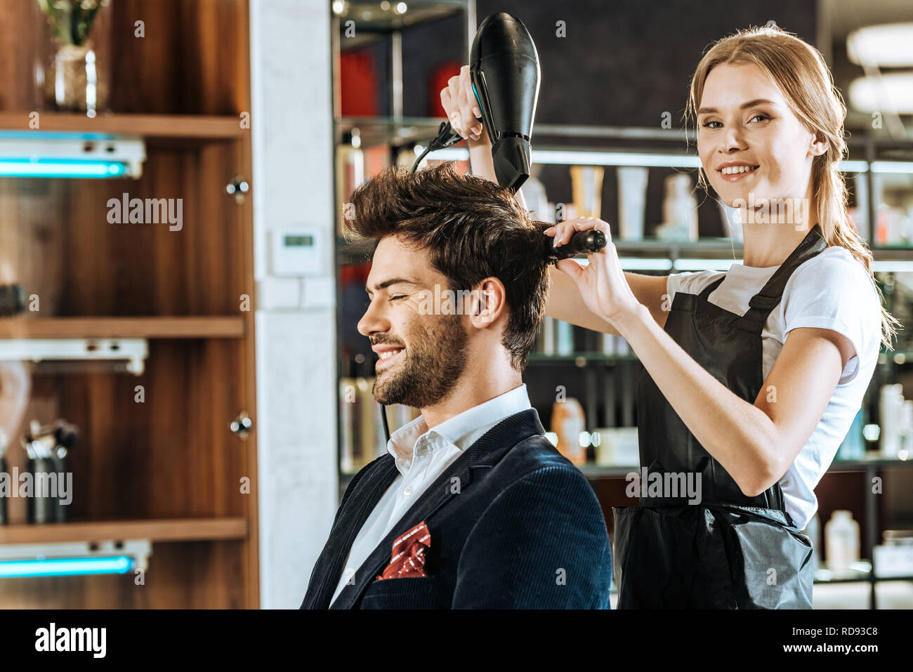 beautiful young hairstylist smiling at camera while drying and combing ... beautiful young hairstylist smiling at camera while drying and combing ...