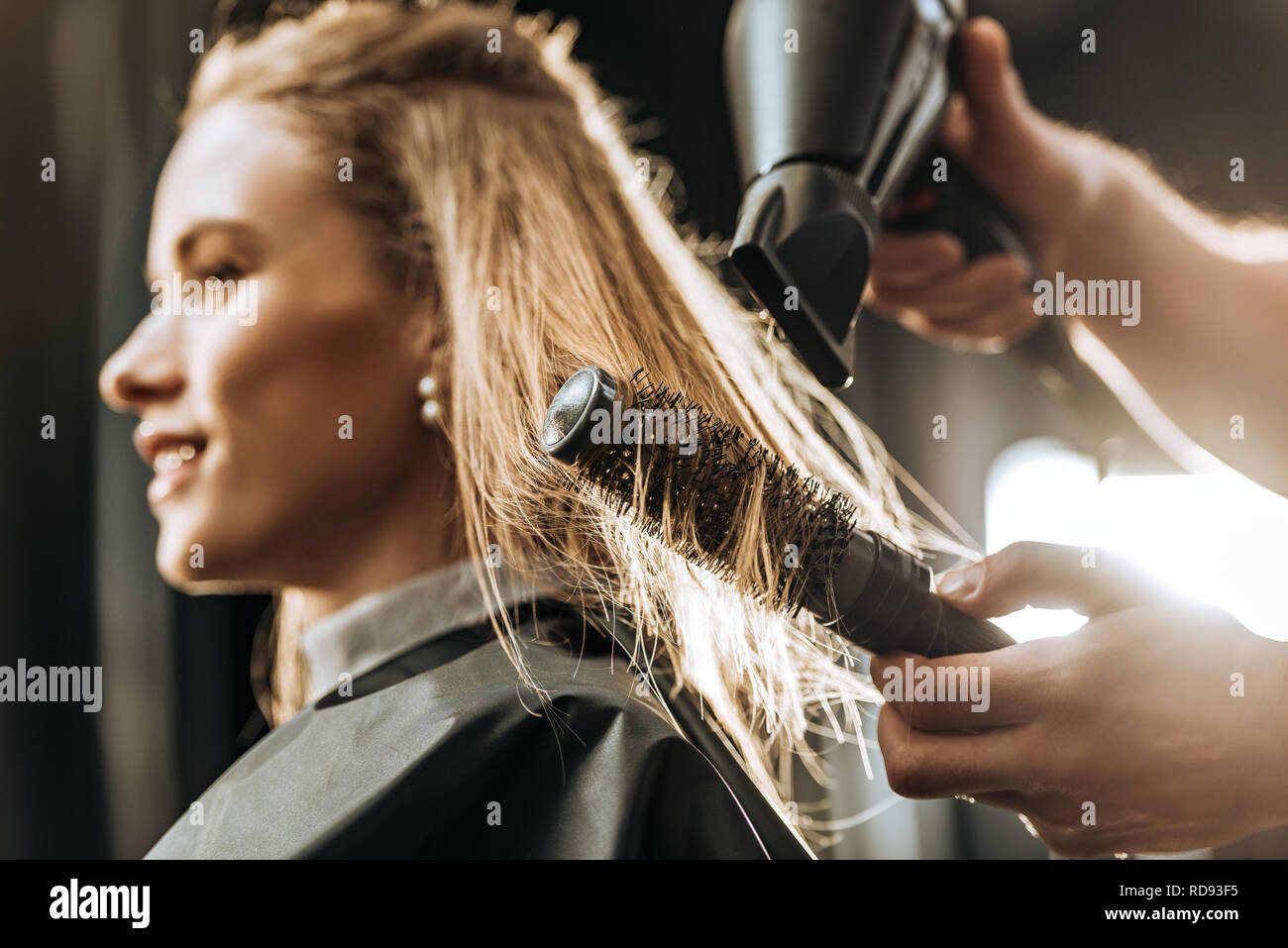 close-up partial view of hairstylist combing and drying hair to ...