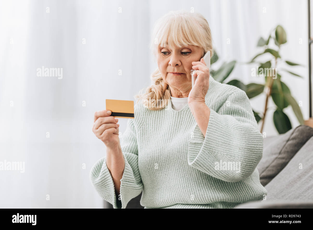 confused senior woman looking at credit card while talking on ...