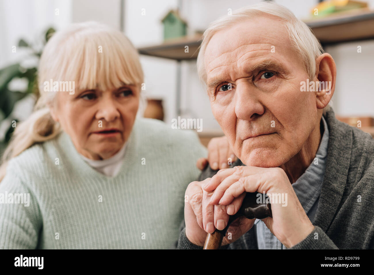 selective focus of sad pensioner sitting near retired wife at home ...