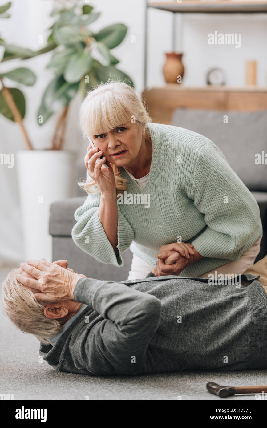 senior woman helping old man with walking stick and looking at camera ...