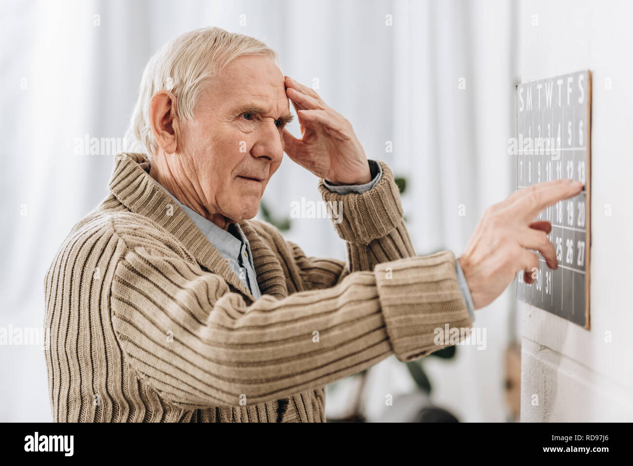 senior man looking at wall calendar and touching head Stock Photo - Alamy
