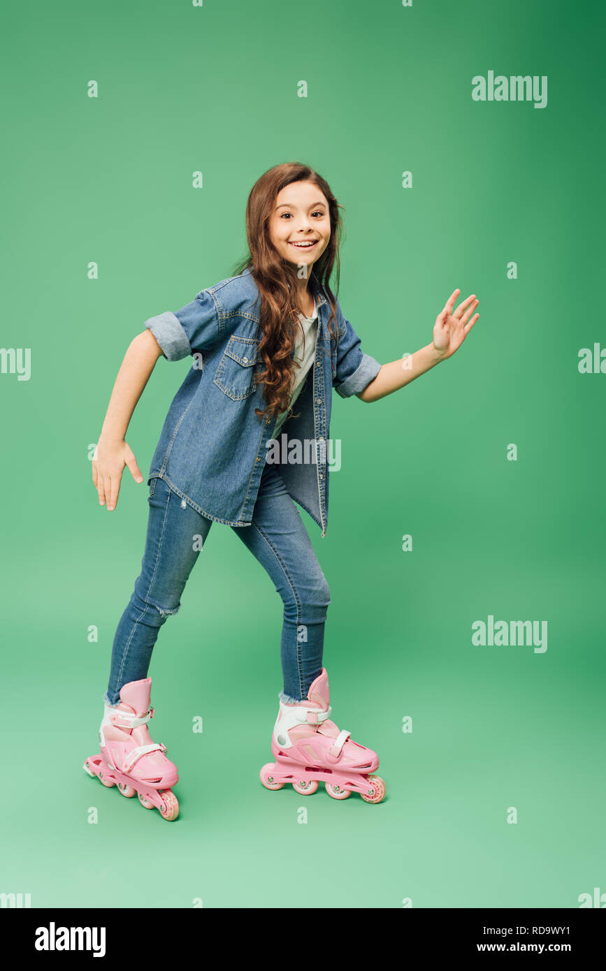 smiling child rollerblading with outstretched hands on green background ...