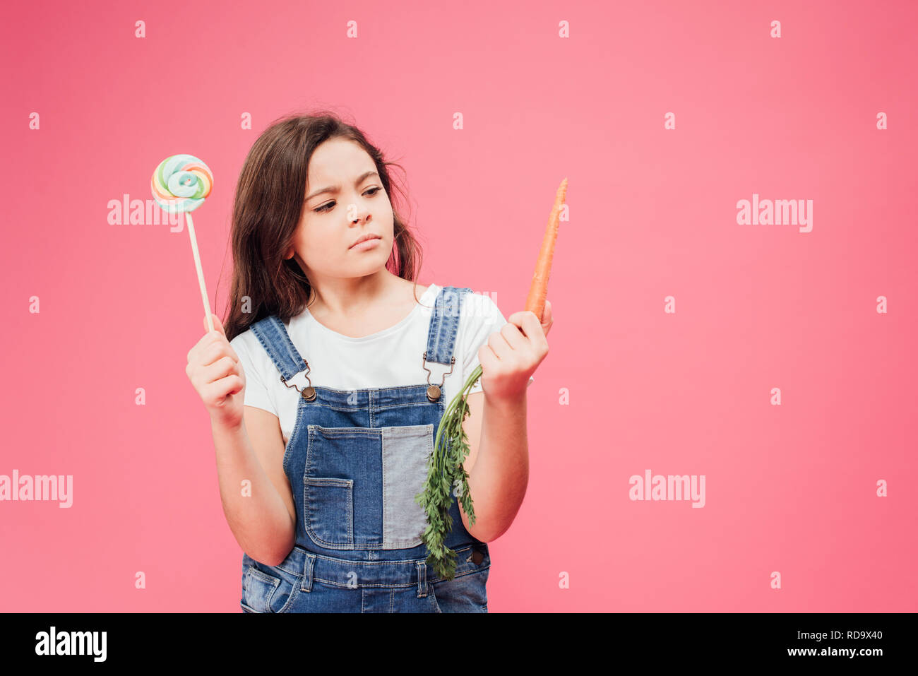 serious child choosing between carrot and candy isolated on pink Stock ...