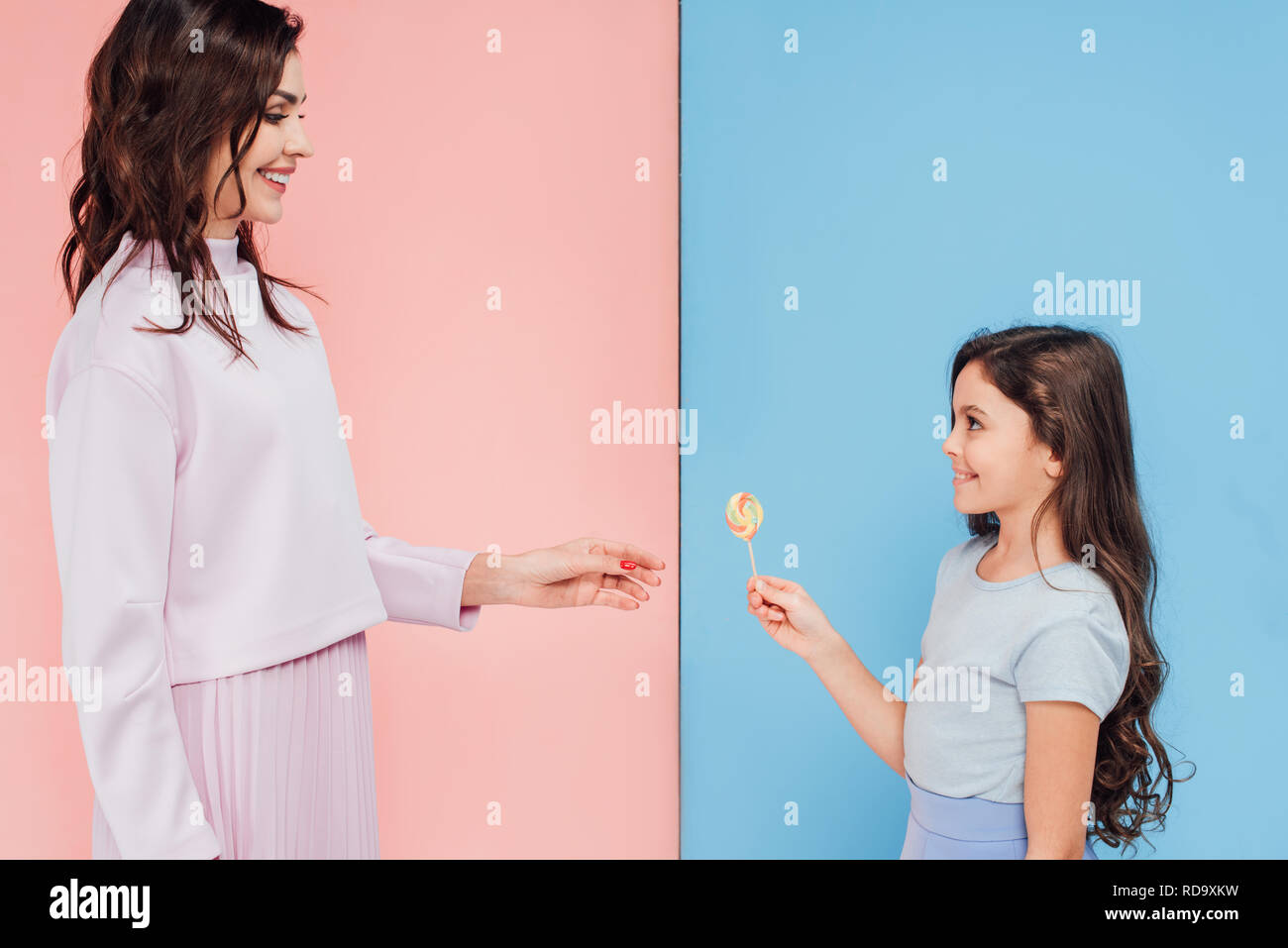 adorable child giving candy to woman on blue and pink background Stock ...