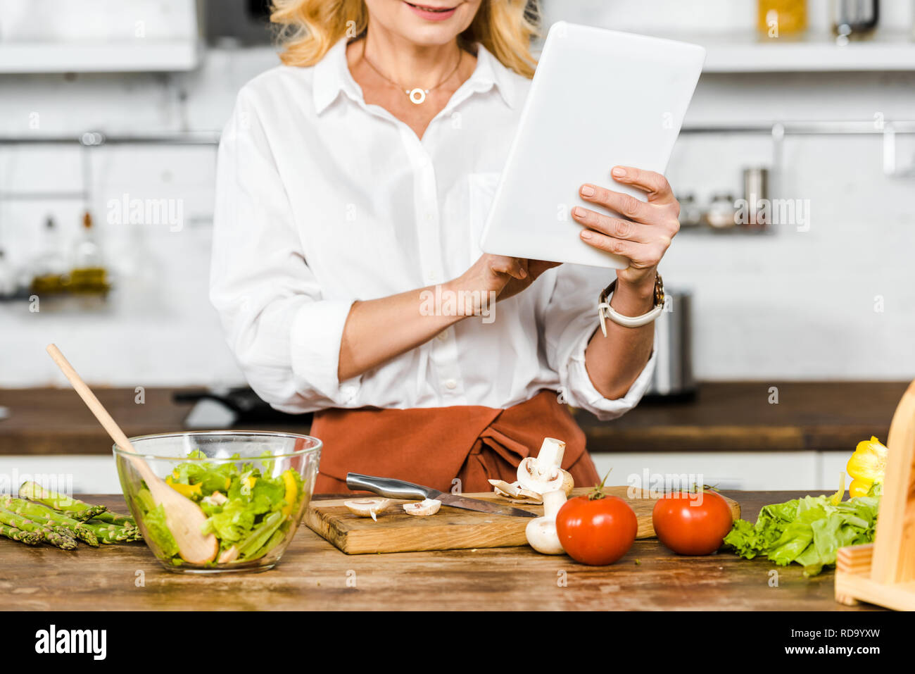 cropped image of mature woman reading recipe from tablet during cooking ...