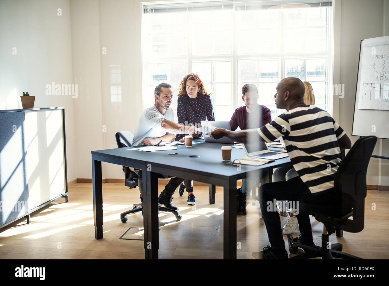 Group of diverse designers discussing paperwork together while sitting ...