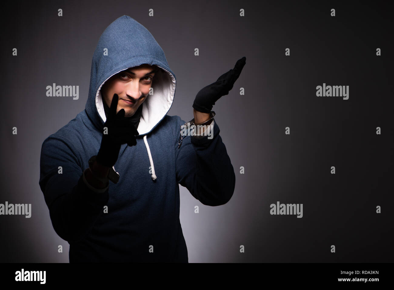 Young gangster in hood on grey background Stock Photo - Alamy